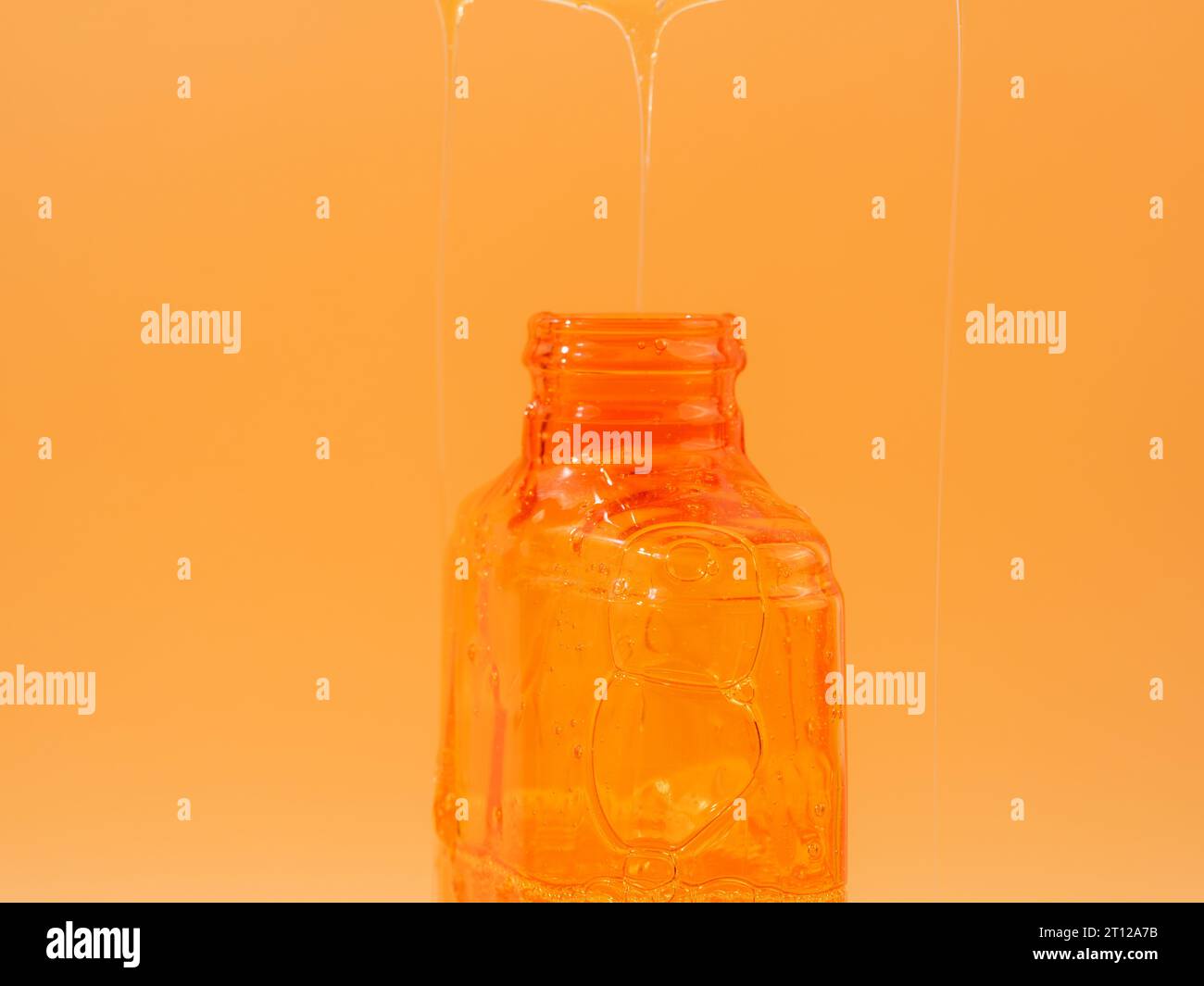 Liquid shower gel gracefully flows into a container on an orange ...