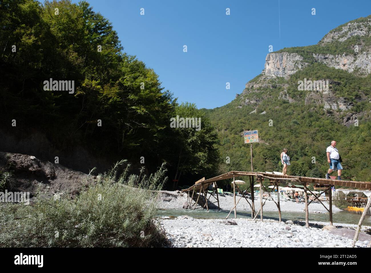 Tourists walking over a makeshift wooden bridge on stilts over shallow ...