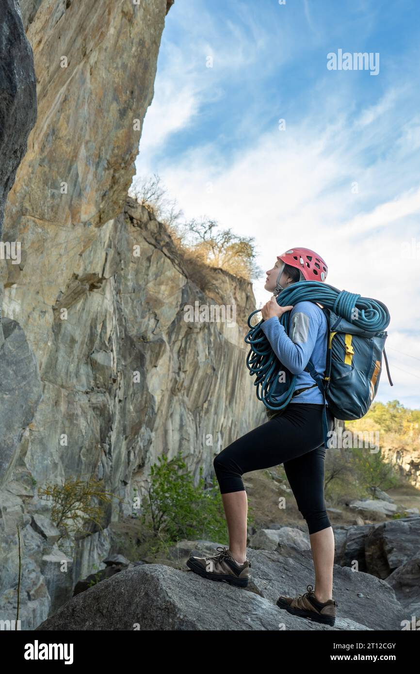 Female climber standing in front of a rock, carrying climbing rope ...