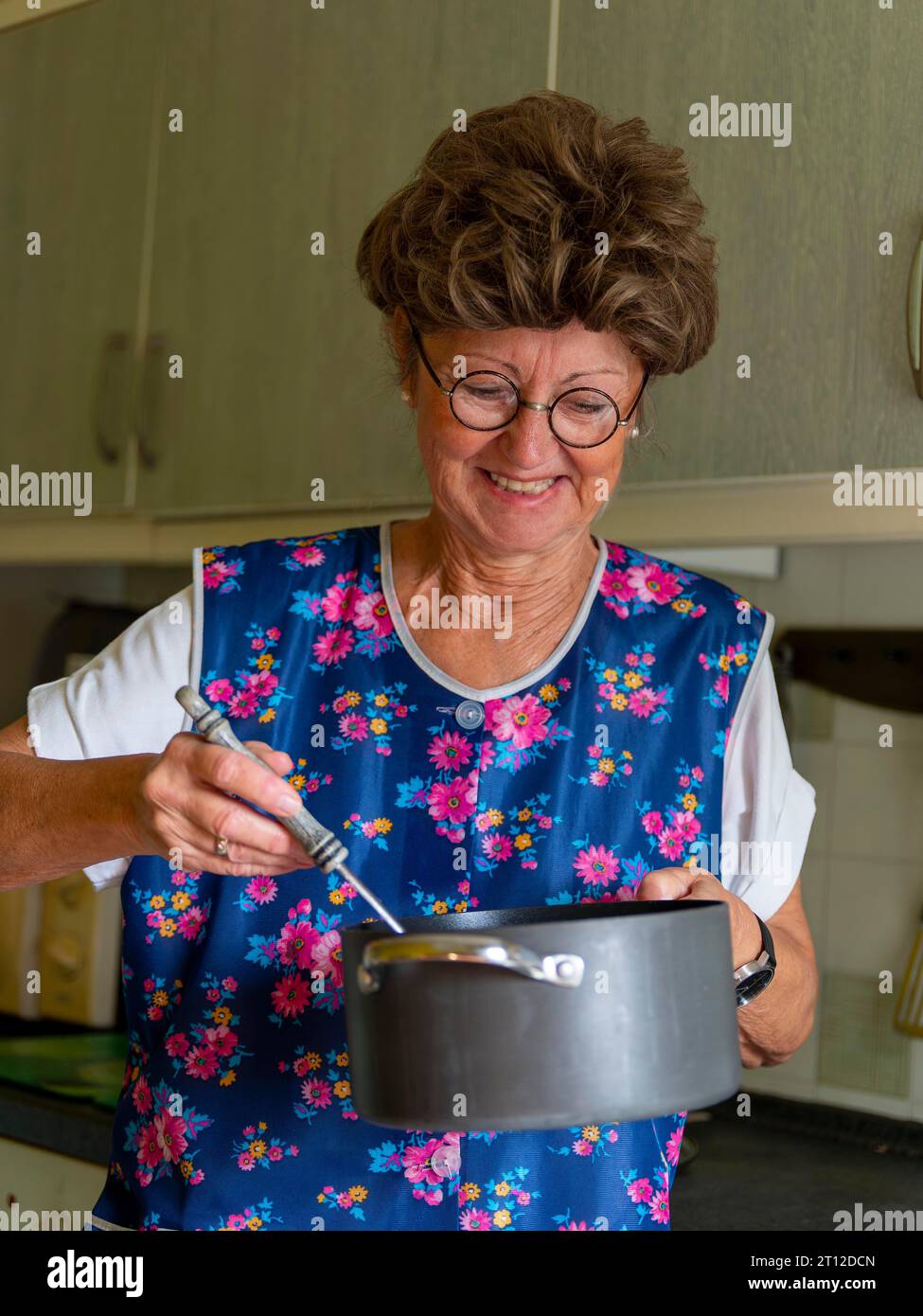 Granny With Old Smock Apron Glasses And Wig In The Kitchen Holding