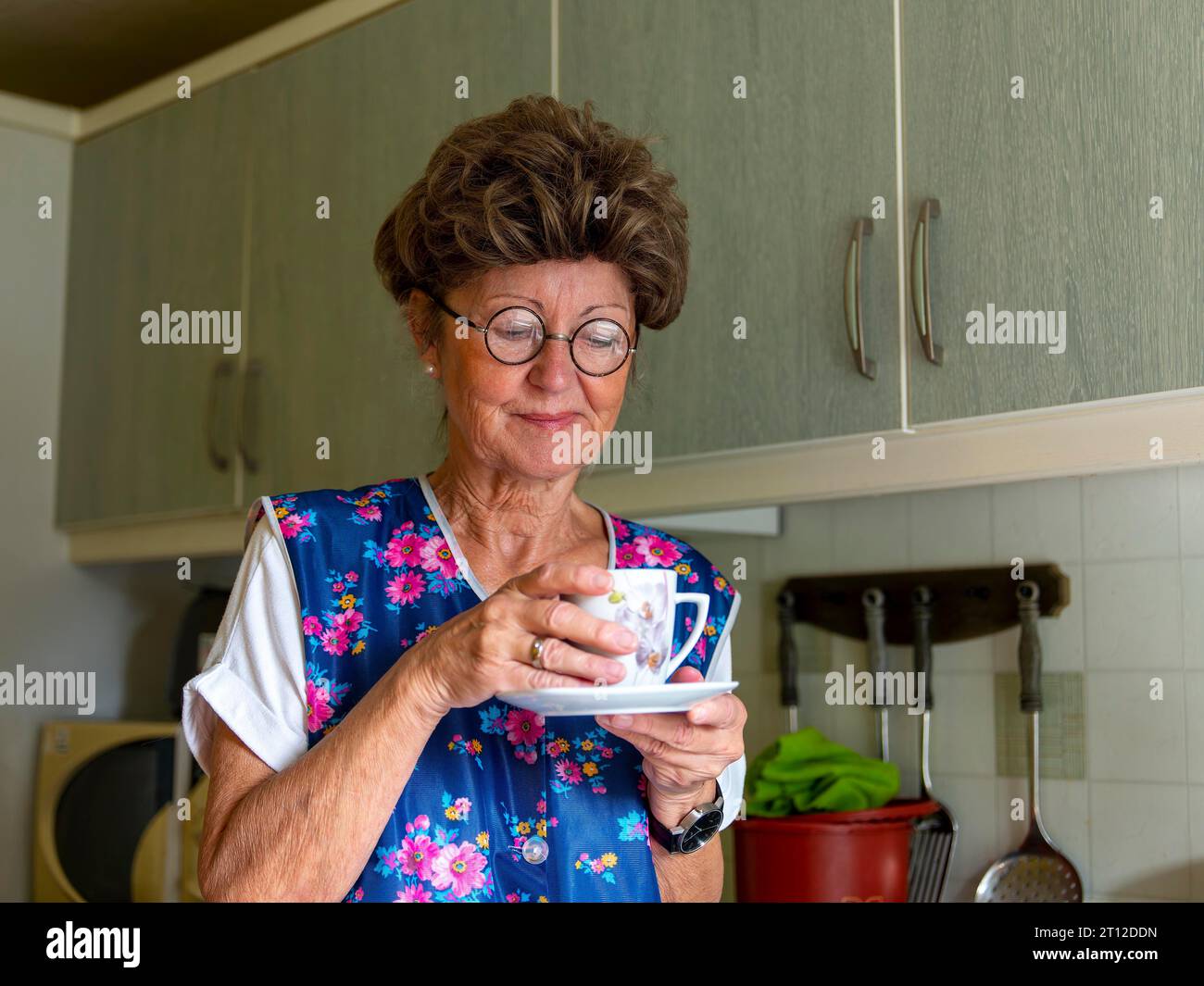 Granny With Old Smock Apron Glasses And Wig In The Kitchen Holding