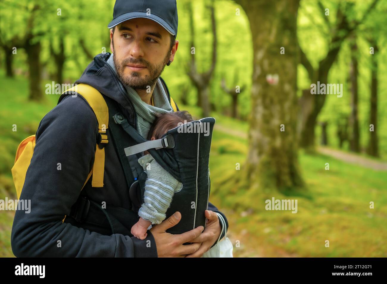 A young father with a yellow backpack and a black cap walking with the ...