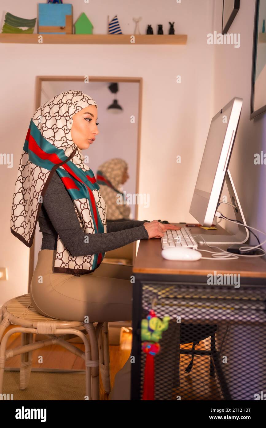 Veiled Arab girl at home computer, working from home. Modern Arab young ...