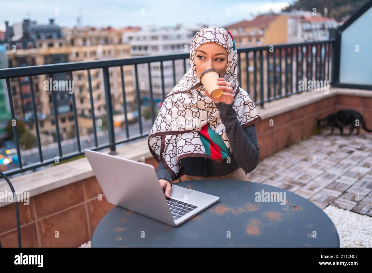 Arab girl with a white veil at the computer on the terrace of a coffe ...