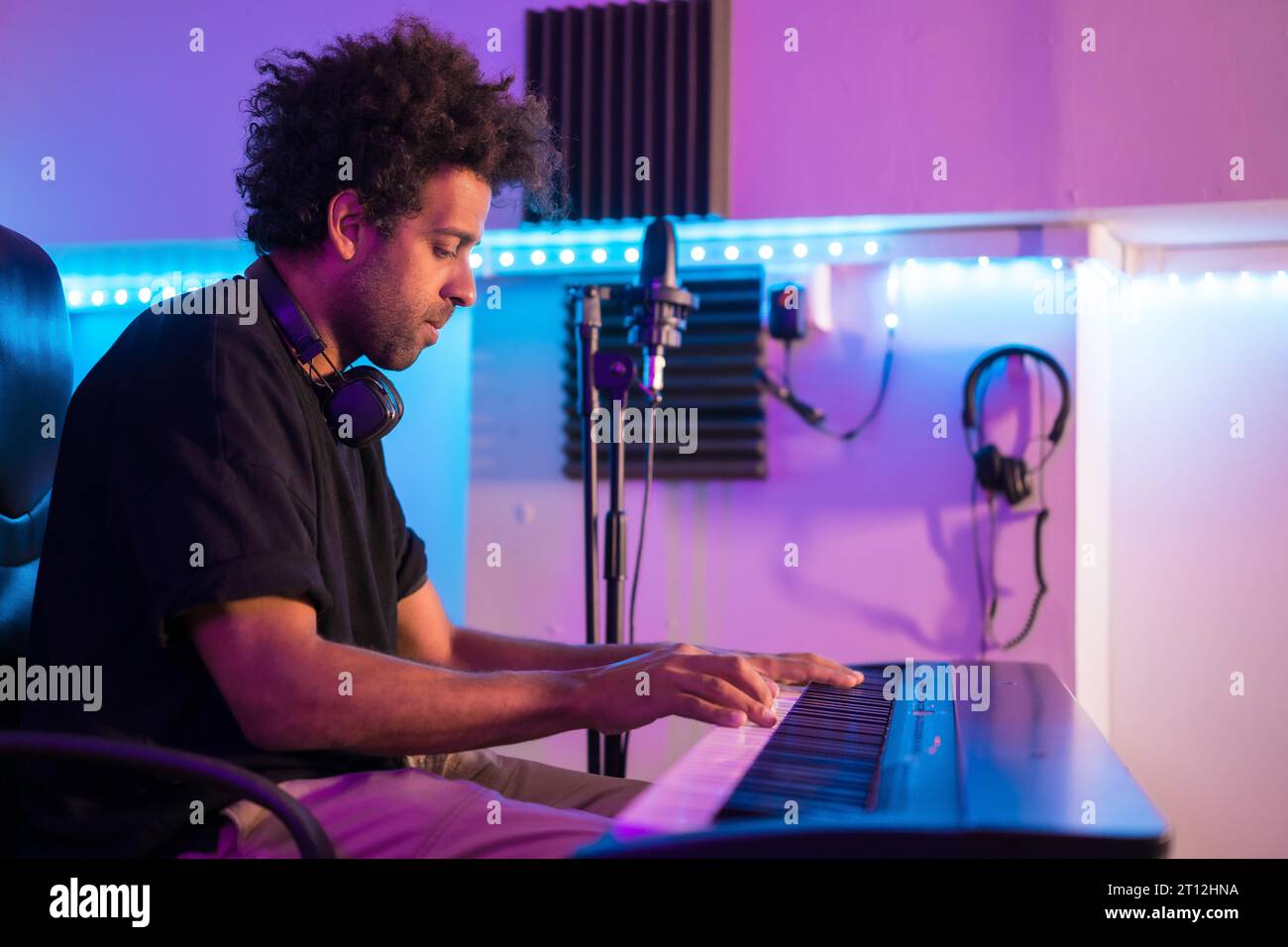 Side view of a musician producer in studio with neon lights creating a ...