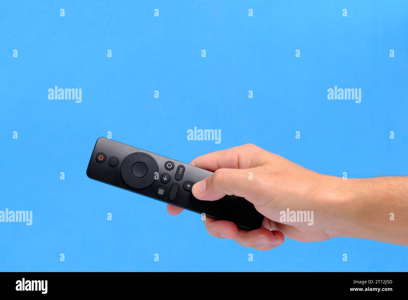 Hand blue background holds TV remote by pressing button with finger ...