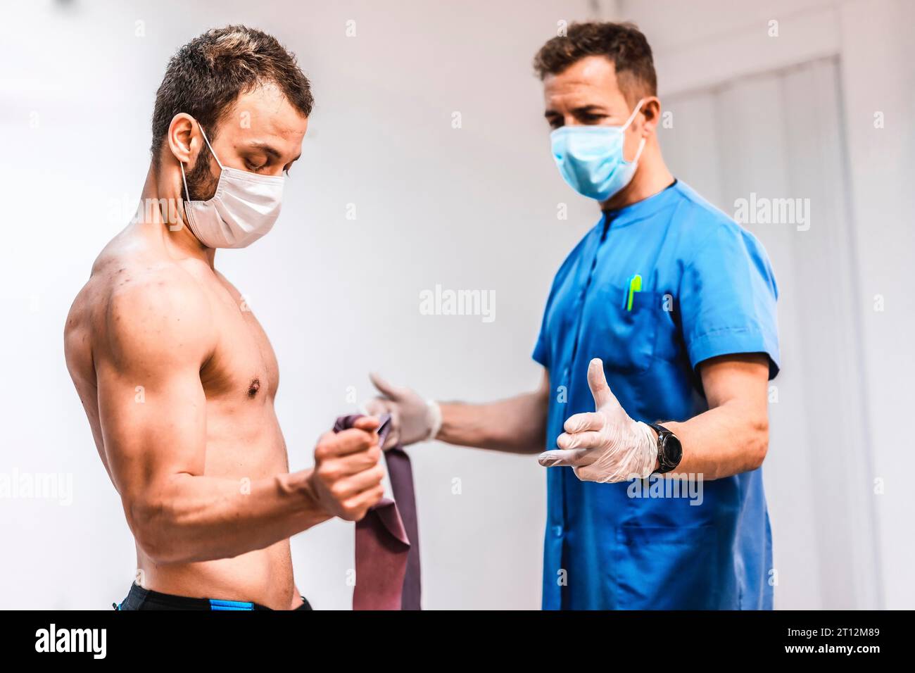 A patient without a shirt and wearing a mask with arm exercises with ...