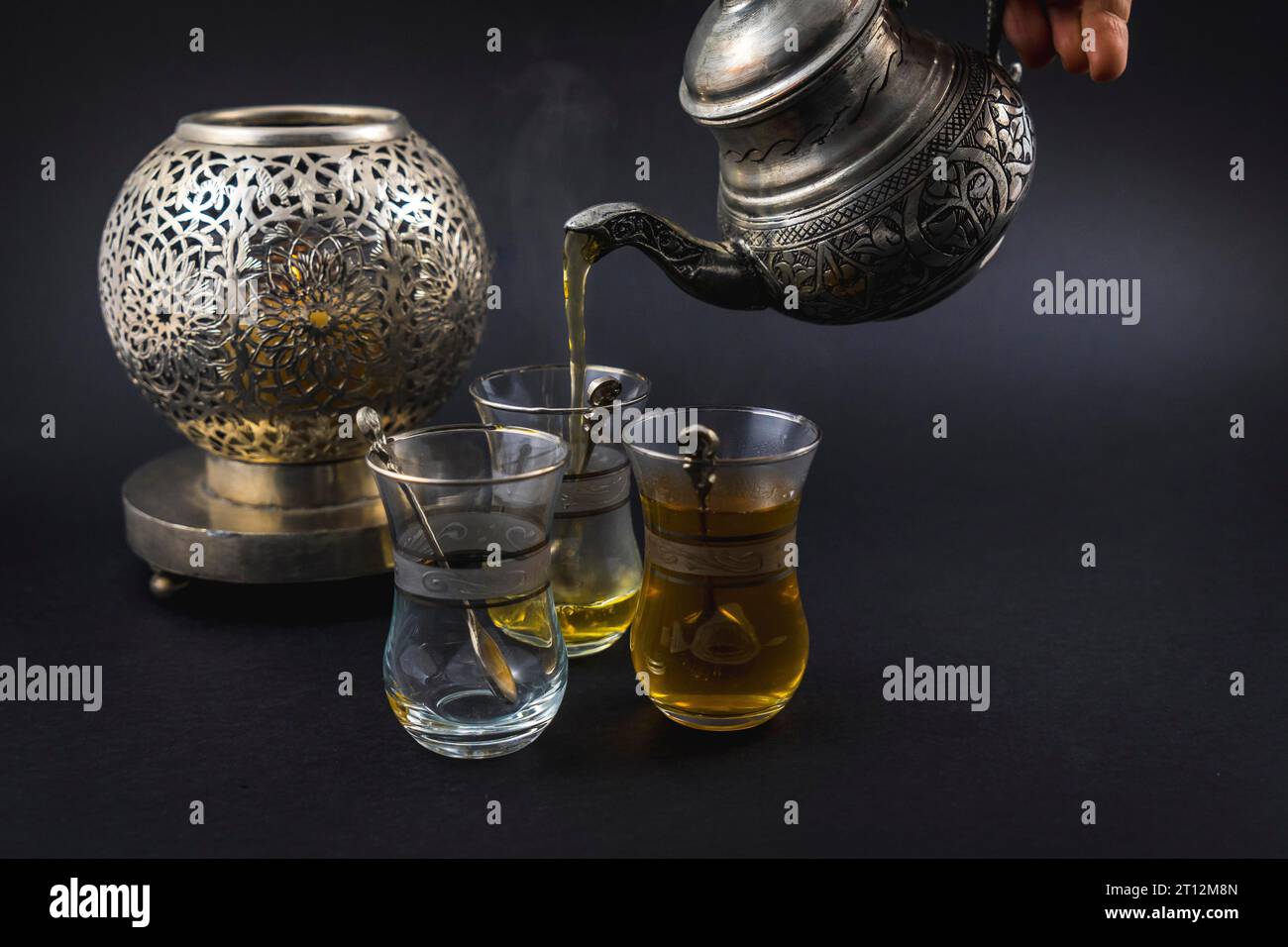Serving Moorish tea from the top of a metal cup to three glasses, a cup ...