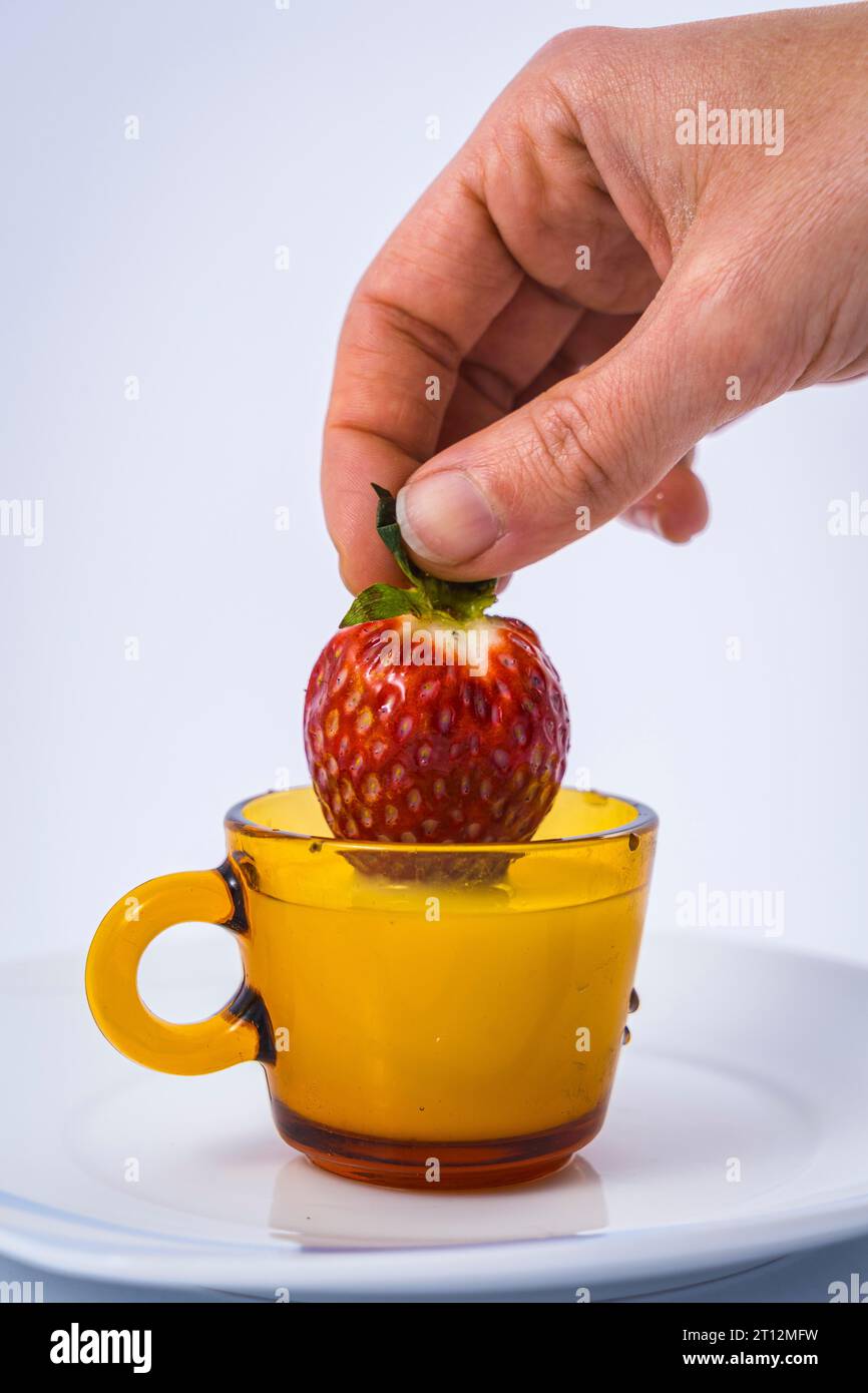 A strawberry inside a milk cup by a woman hand with white background ...