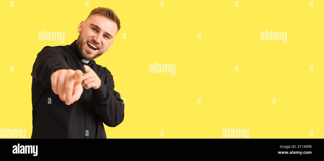 Young priest pointing at viewer against yellow background with space ...