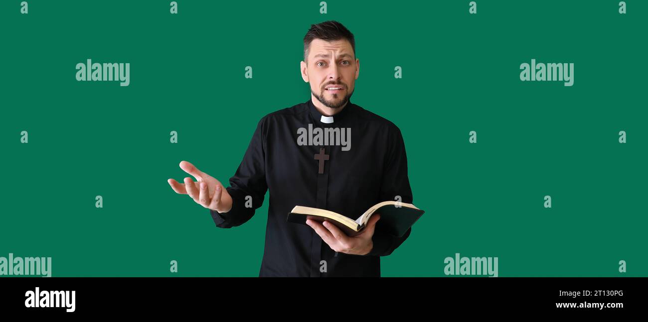Confused priest with Bible on green background Stock Photo - Alamy