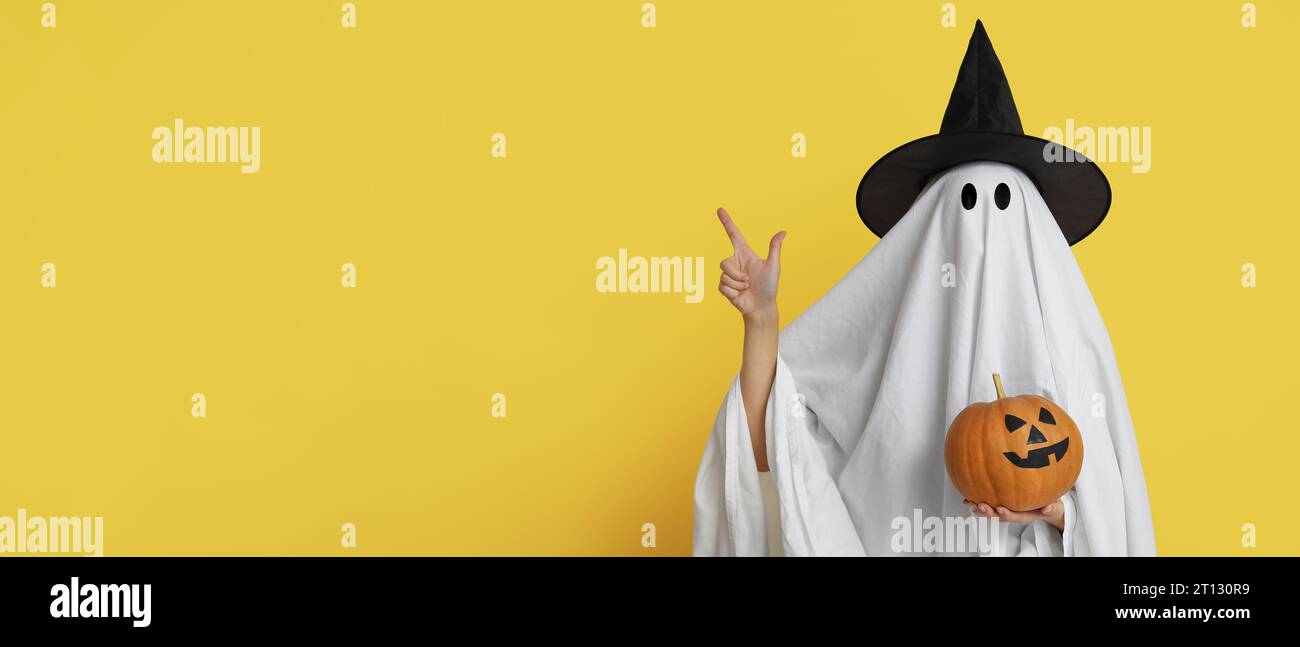 Person in costume of ghost holding Halloween pumpkin and pointing at ...