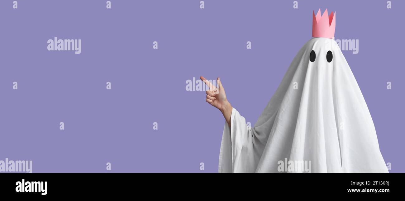 Person in costume of ghost pointing at something on lilac background ...