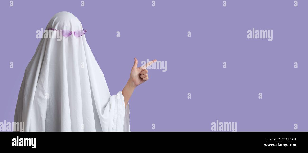 Person in costume of ghost pointing at something on lilac background ...