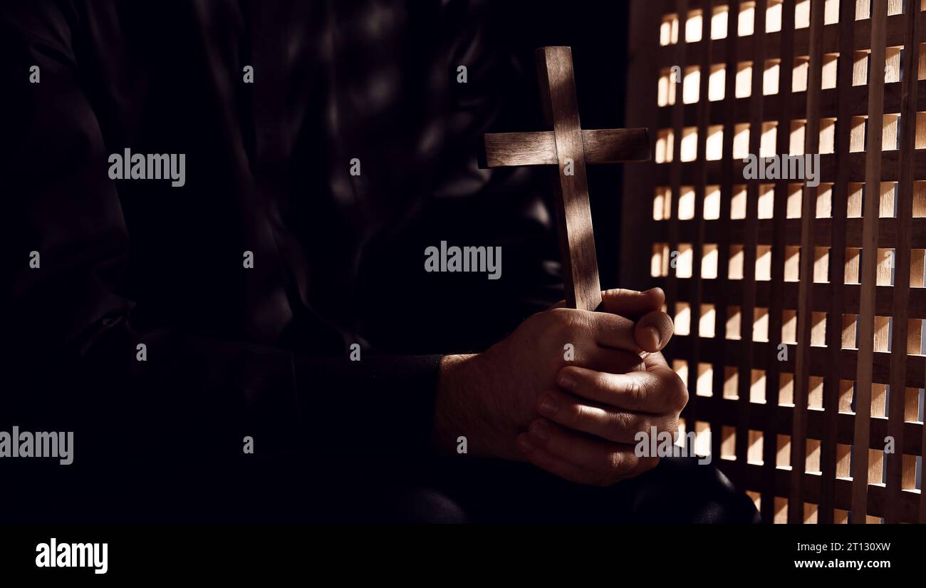 Young priest with cross in confession booth Stock Photo - Alamy