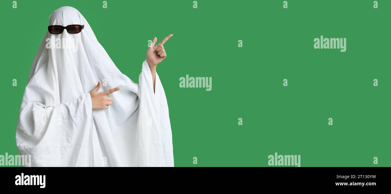 Person in costume of ghost pointing at something on green background ...