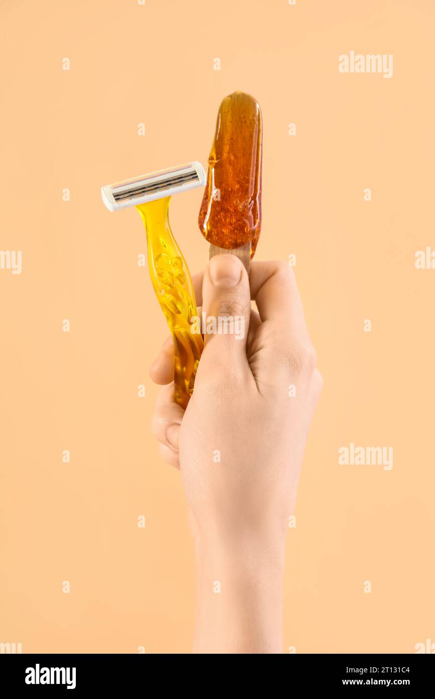 Female hand holding spatula with sugaring paste and razor on beige ...