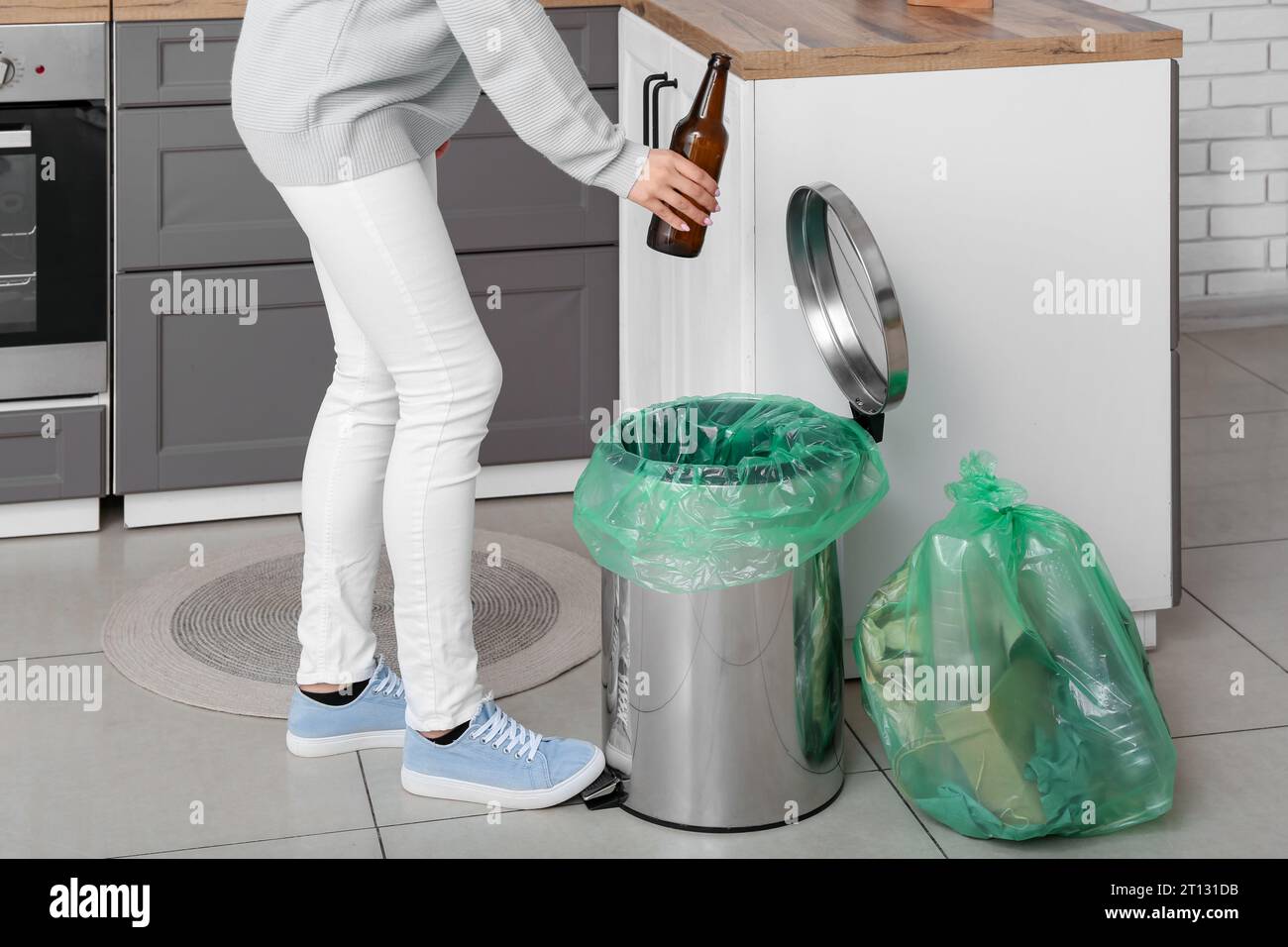 Woman putting glass bottle into trash bin near full garbage bag in ...