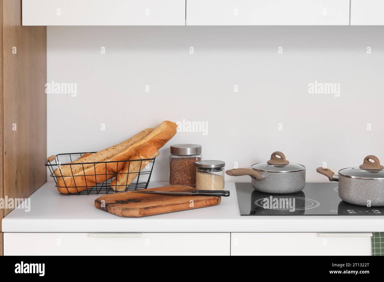 White kitchen counters with cutting board, electric stove, cooking pots ...