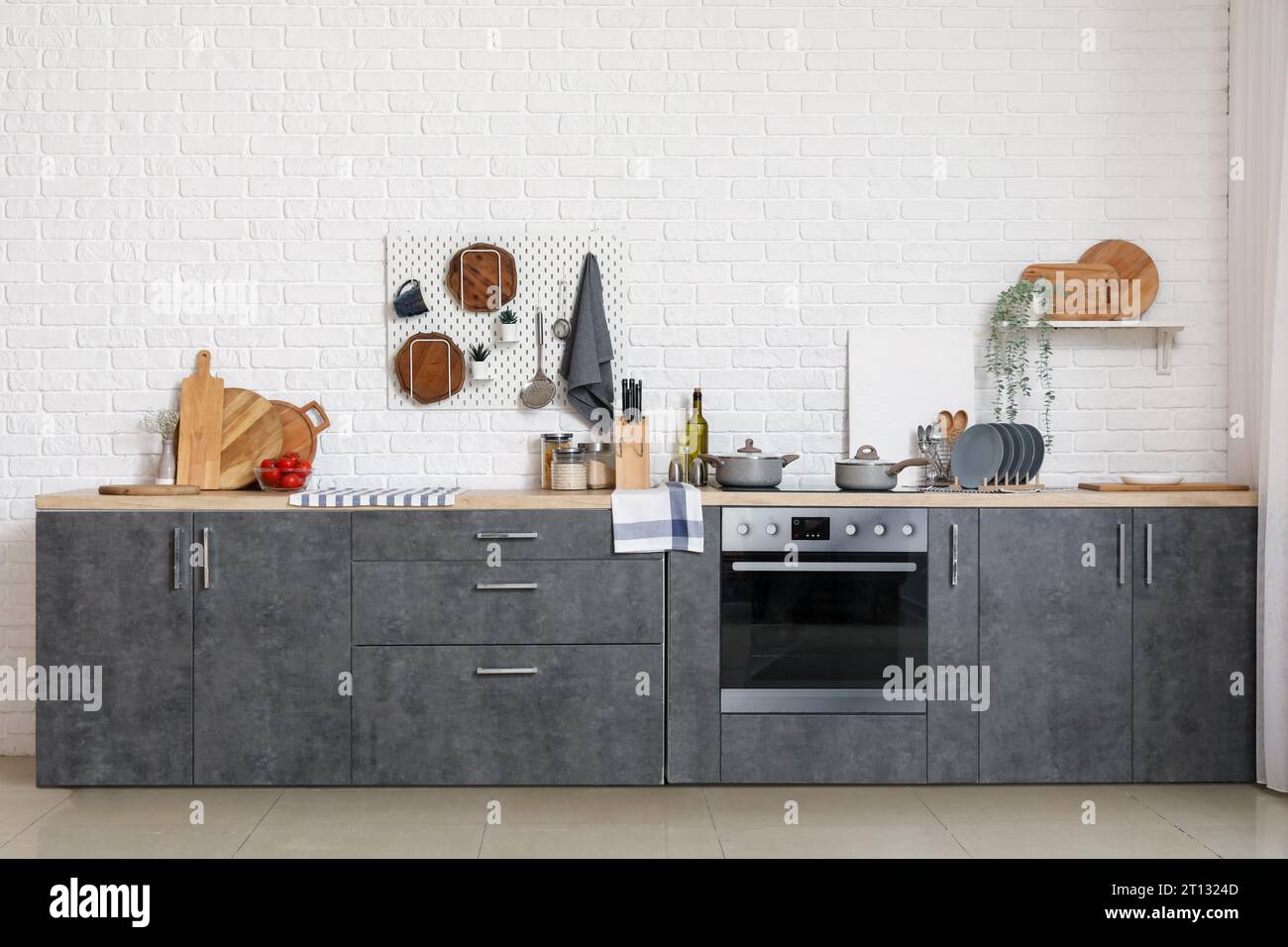 Grey counters with cutting boards, utensils, oven and electric stove in ...