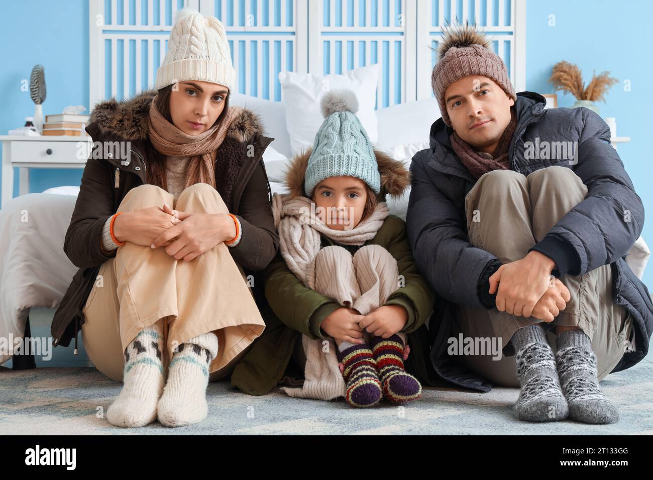 Frozen family wearing winter clothes in bedroom with lack of heating ...