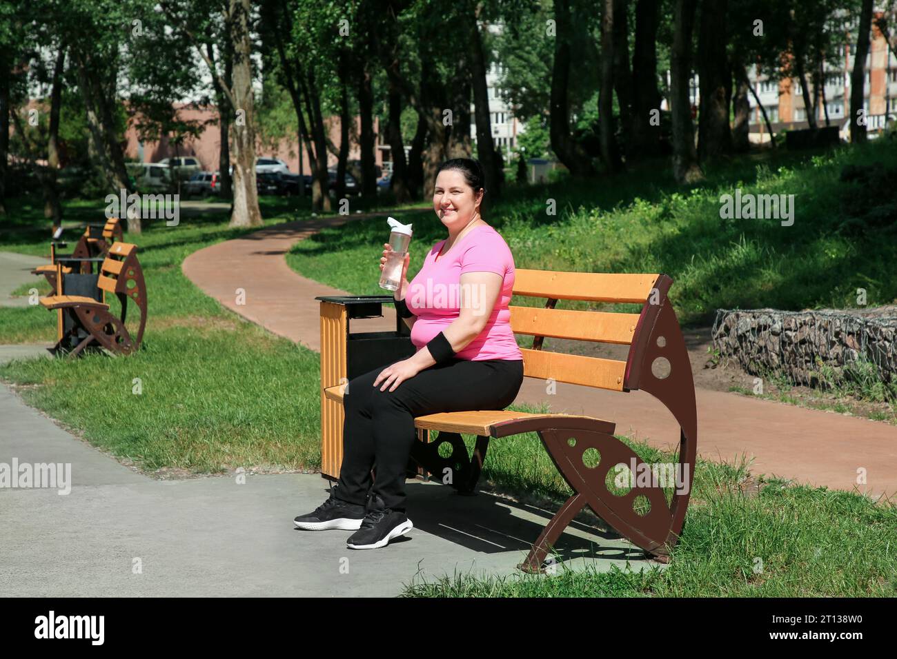 Overweight woman with bottle of water sitting on bench in park Stock ...