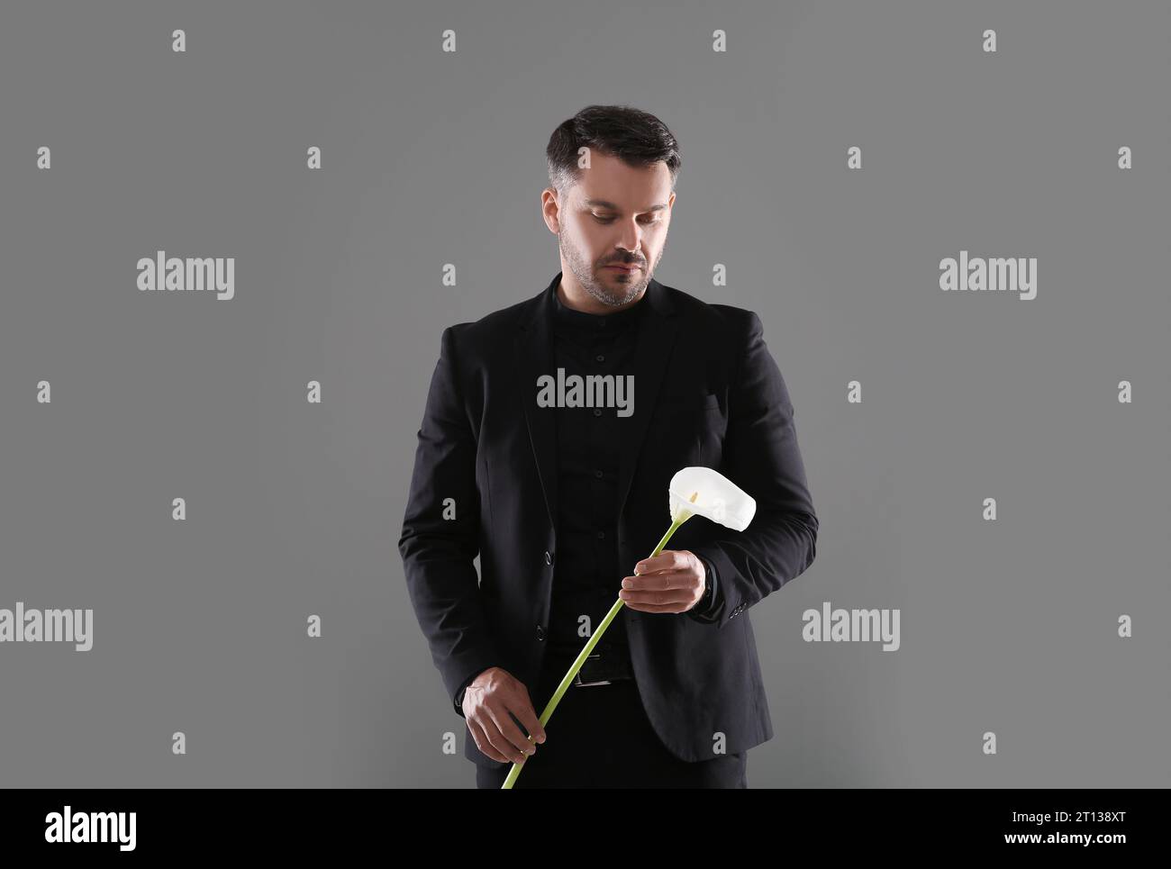 Sad man with calla lily flower on grey background. Funeral ceremony ...