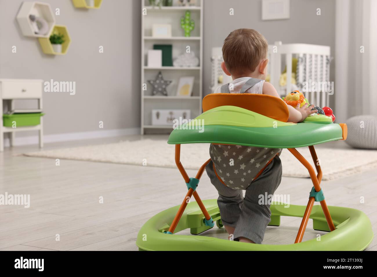 Cute baby making first steps with toy walker at home, back view. Space ...
