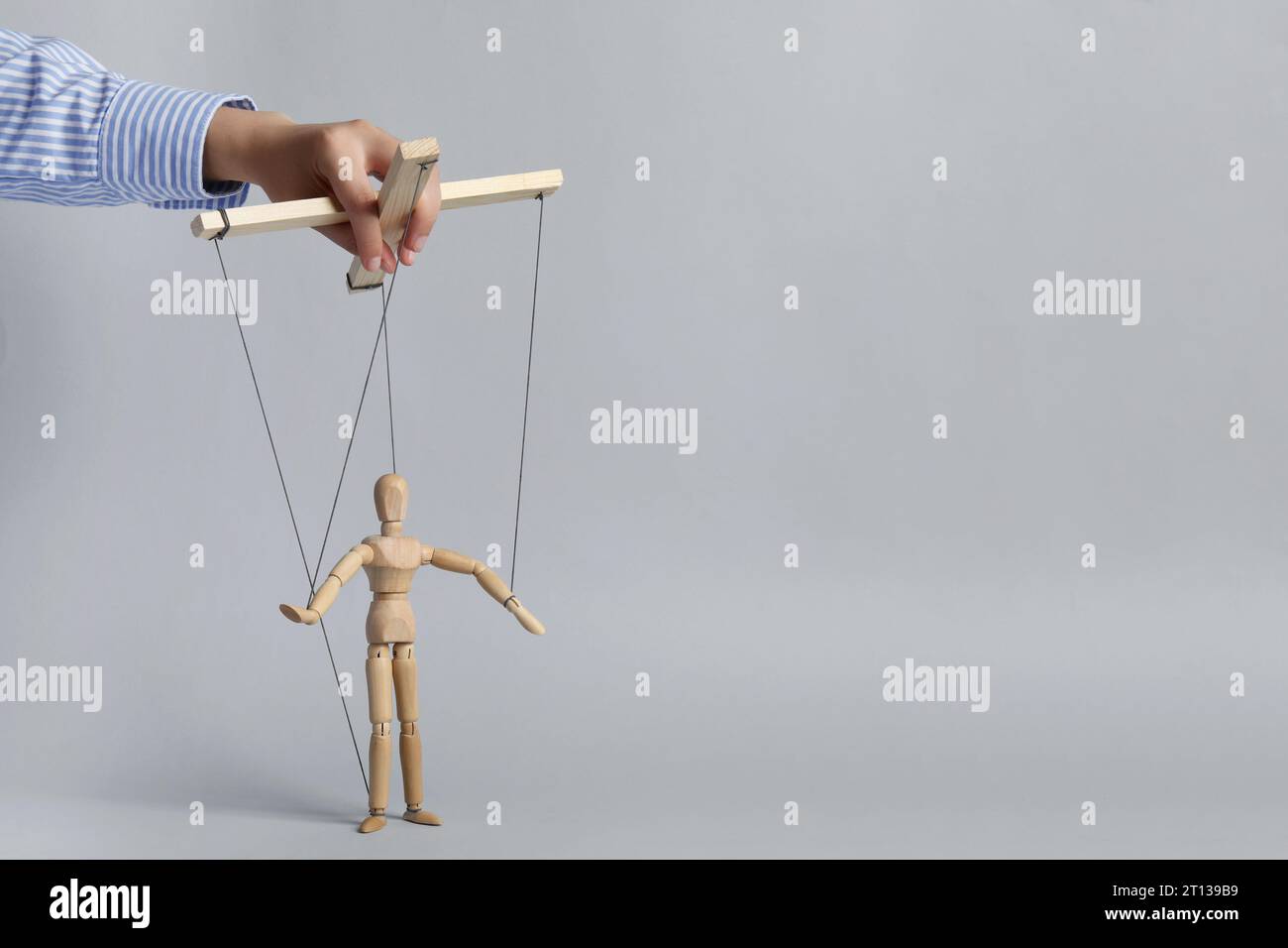Woman pulling strings of puppet on light grey background, closeup ...