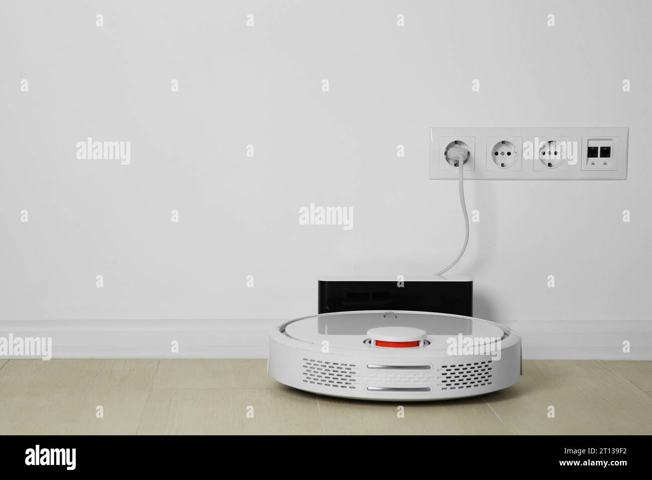 Robotic vacuum cleaner charging from electric socket on floor indoors ...