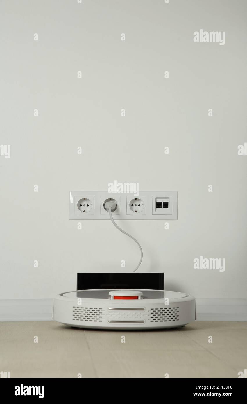 Robotic vacuum cleaner charging from electric socket on floor indoors ...