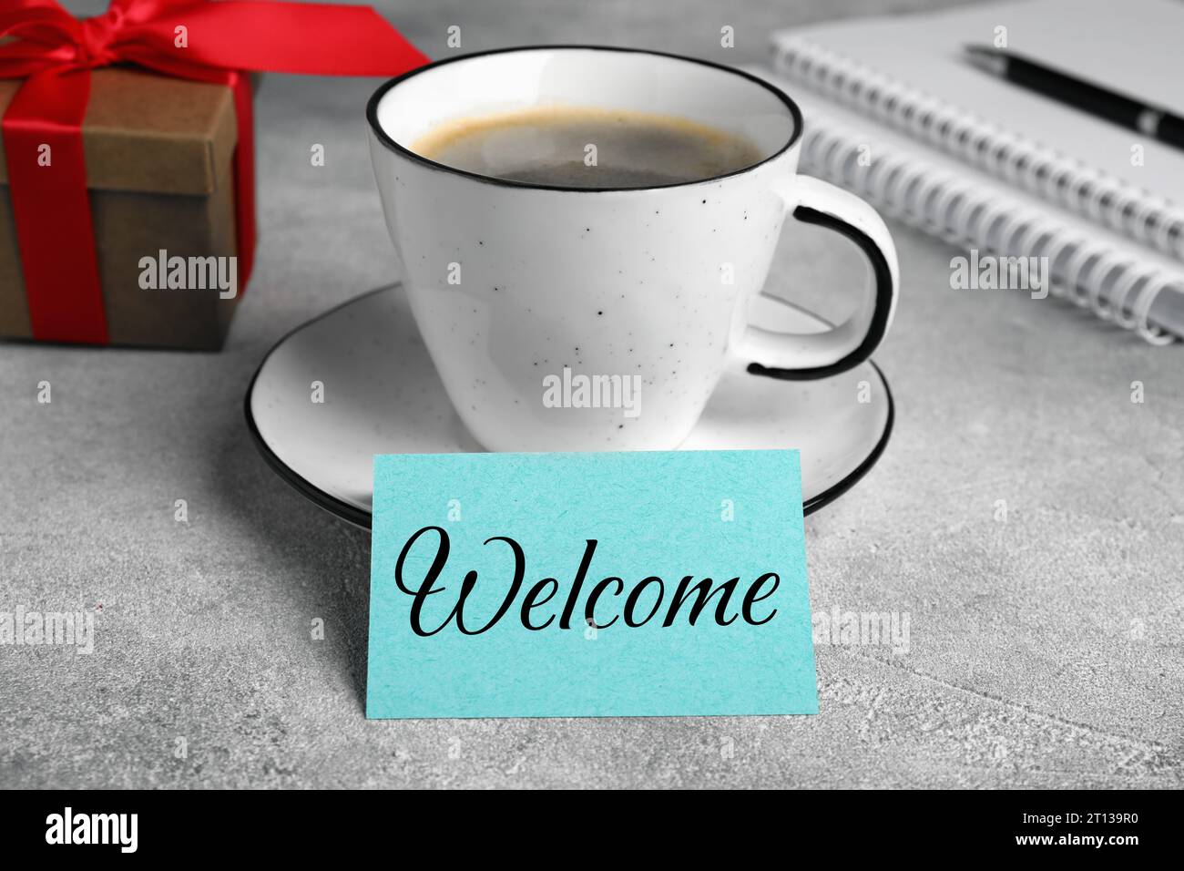 Paper note with word Welcome, cup of coffee and gift box on office desk ...