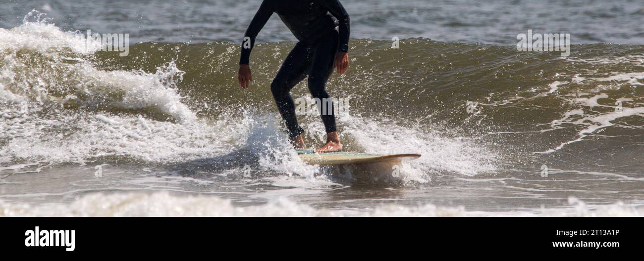 Front view of a man wearing a black wetsuit surfing at Gilgo Beach on ...