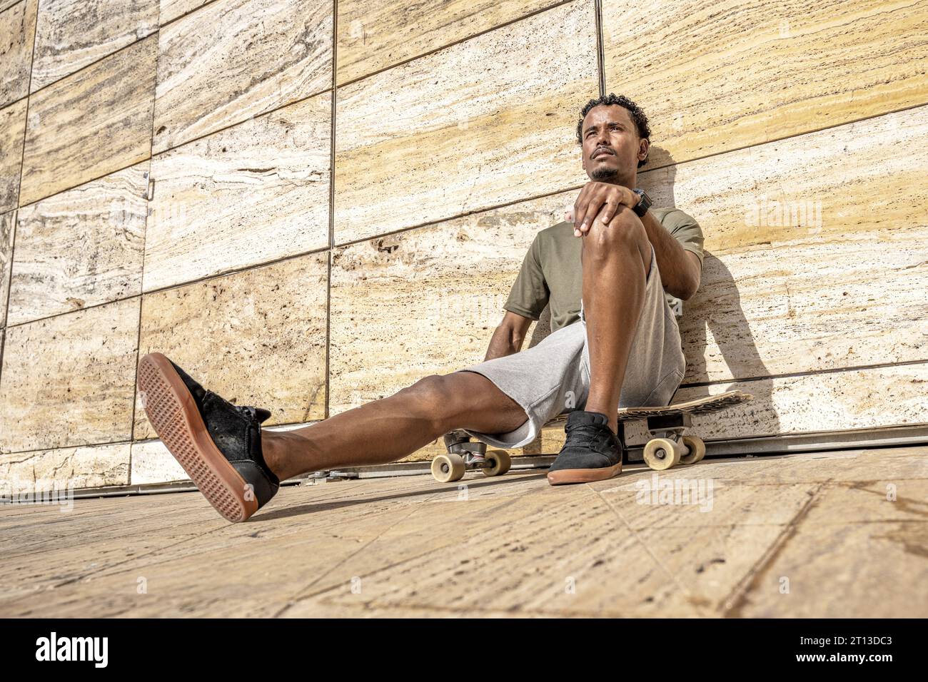 Surf skater resting sitting on his skateboard in an urban scene Stock ...