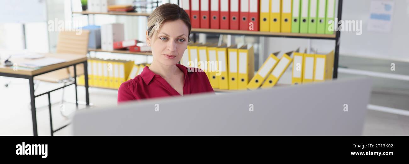 Blonde woman sits at table behind big computer monitor Stock Photo - Alamy