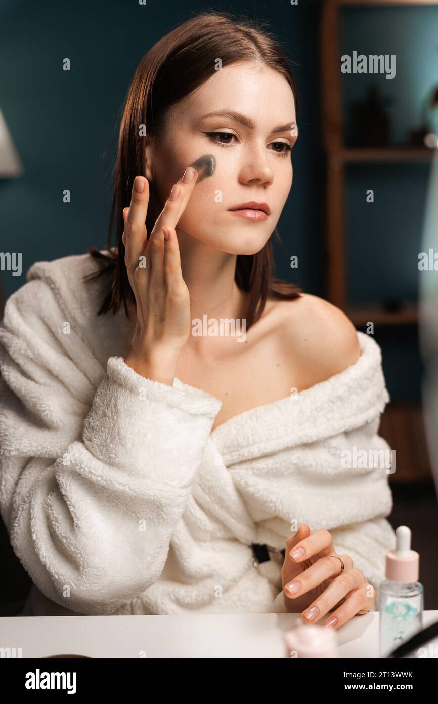 Cute girl applying facial charcoal mask. Young woman using skin care ...