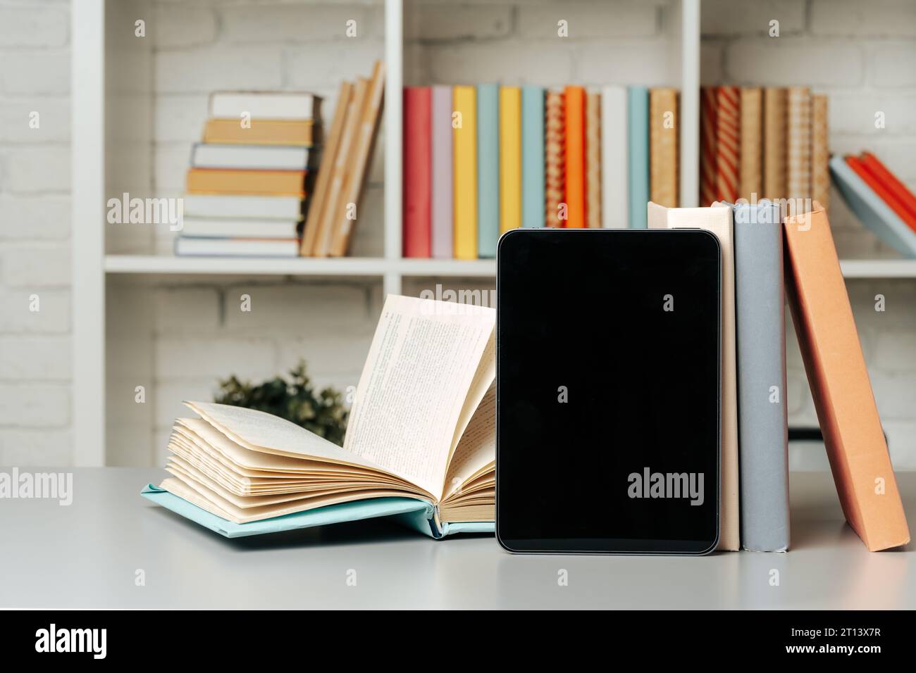 Digital tablet with stacked books in library Stock Photo - Alamy