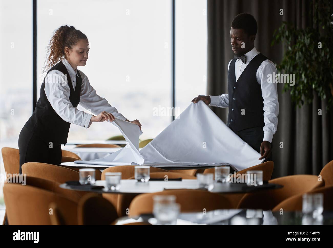 Side view portrait of two elegant servers setting tables with white ...