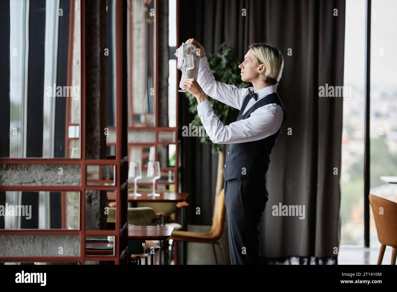 Side view portrait of elegant waiter polishing glasses in luxury ...