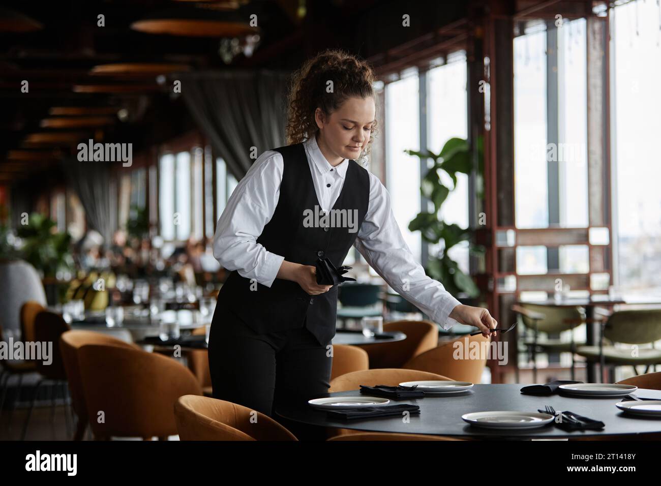 Portrait of young woman as female server setting tables in luxury ...