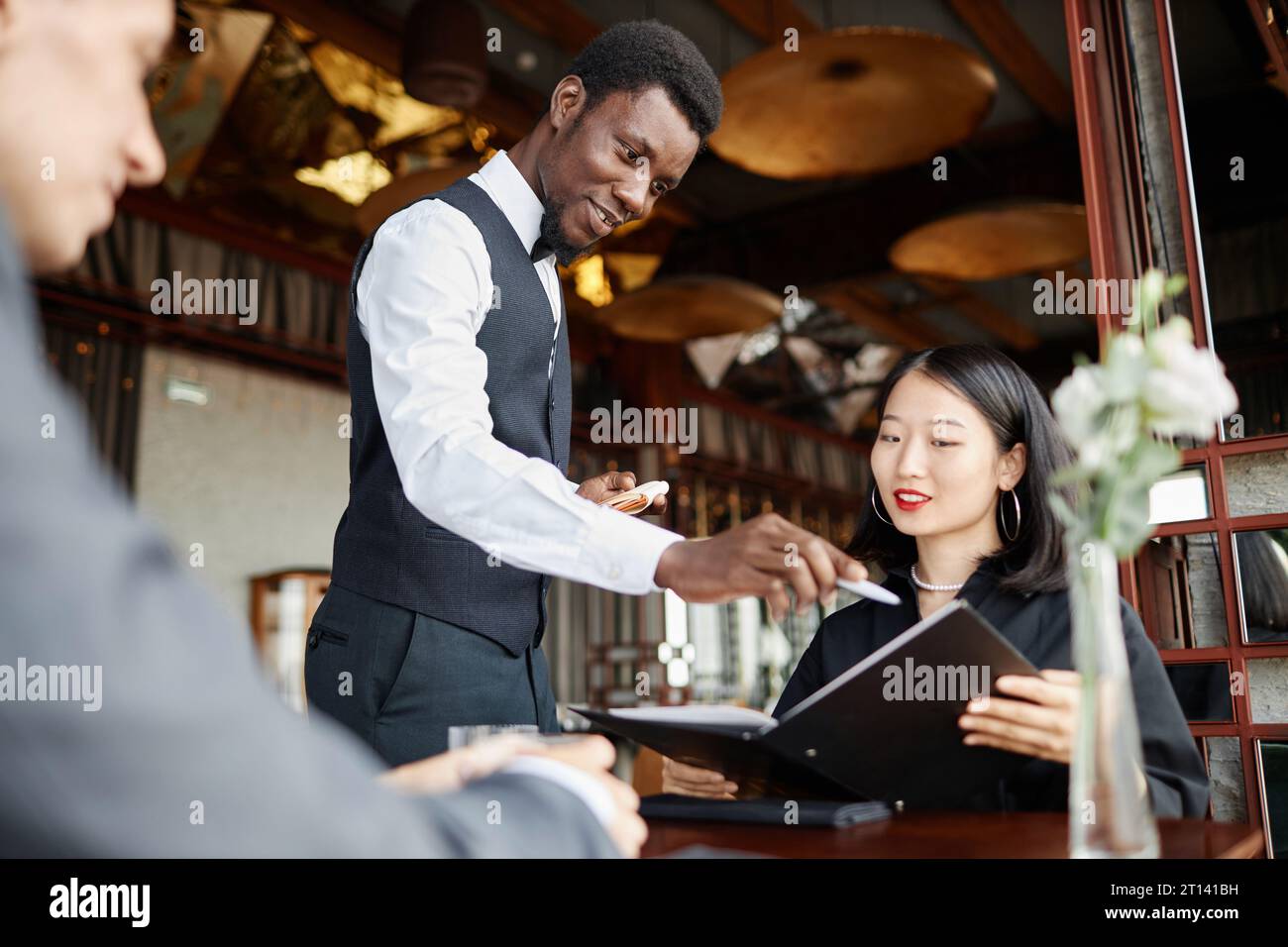 Portrait of Black young man as server taking orders from female gust ...