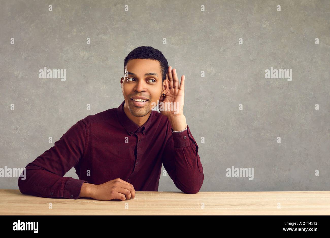 Interested dark-skinned young man raises his hand to his ear ...