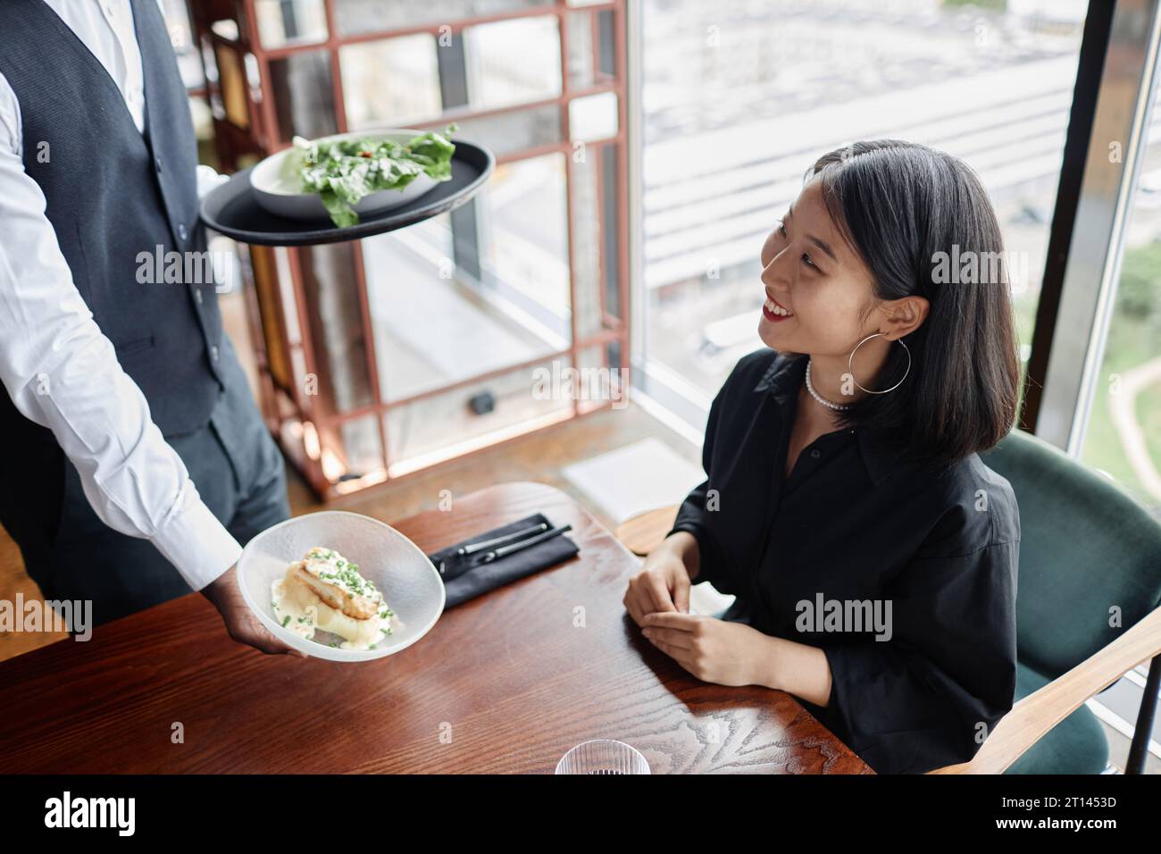 Server bringing food on tray to young woman enjoying dinner in ...