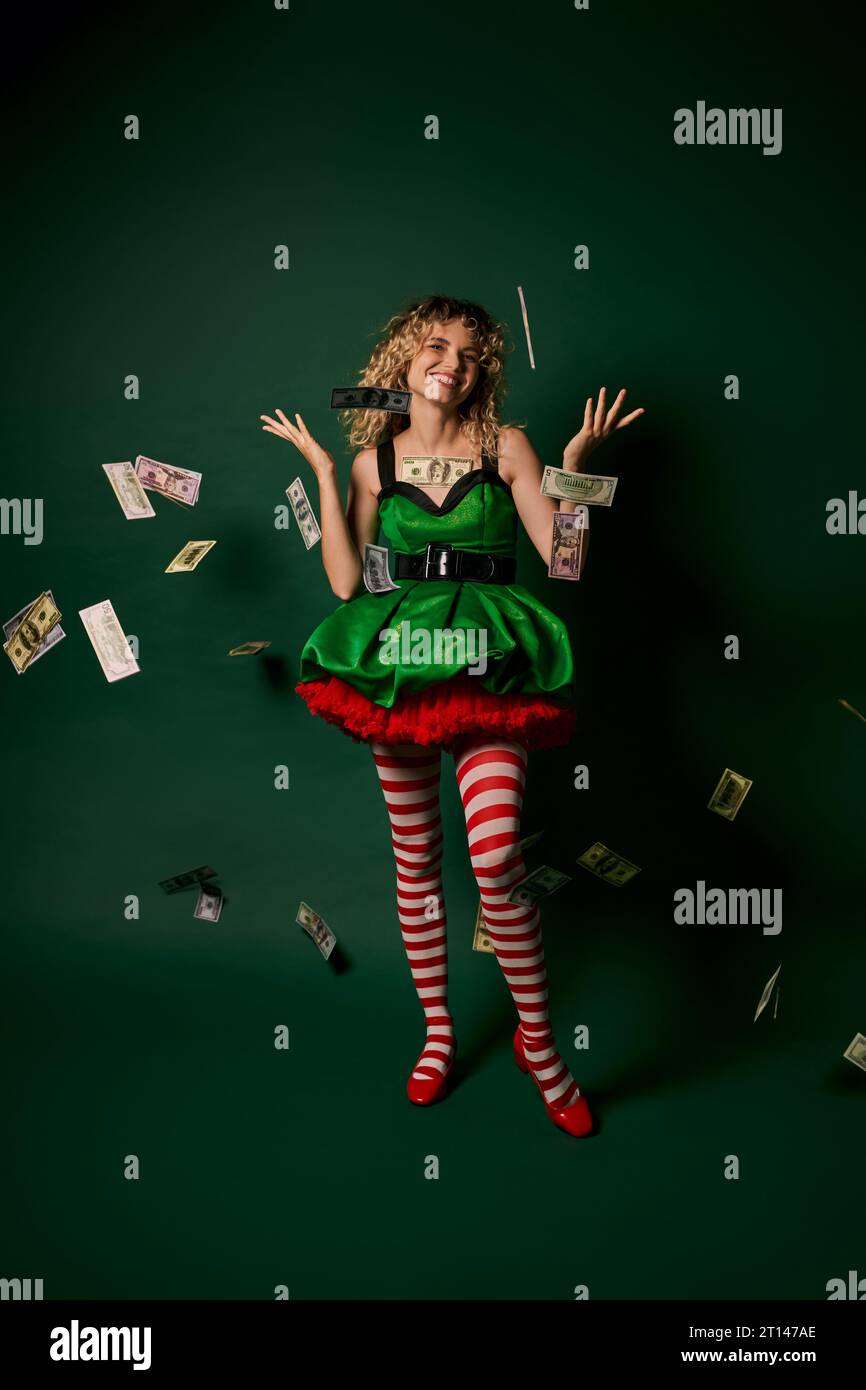cheerful curly woman dressed as new year elf standing under money rain ...