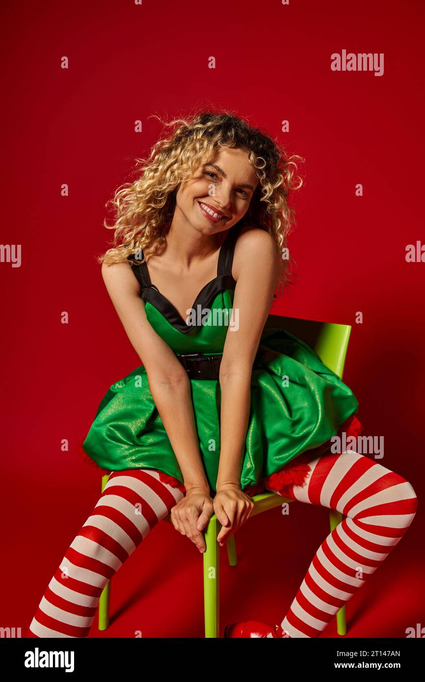 happy curly new year elf in festive dress smiling and sitting on yellow ...