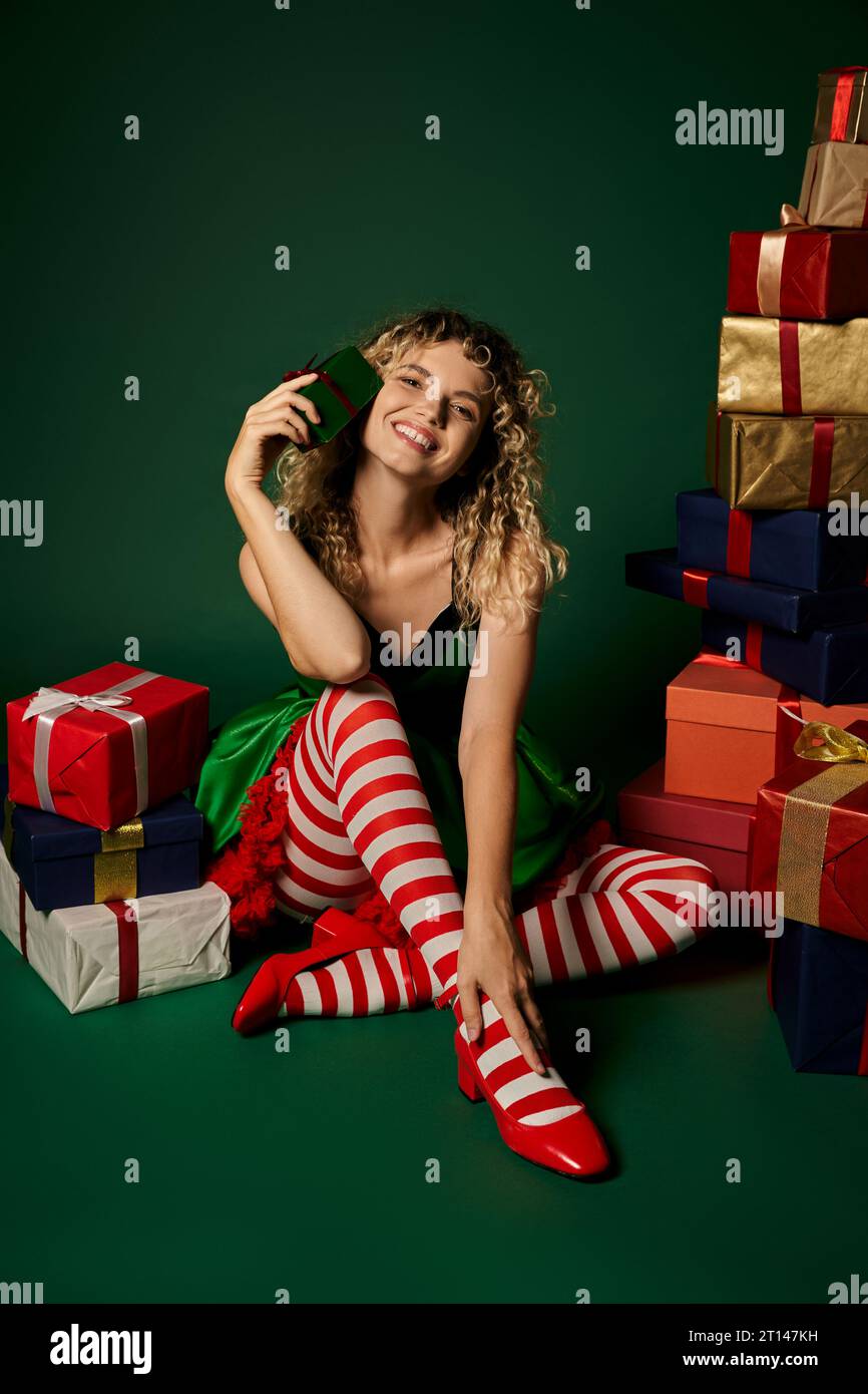 cheerful new year elf in green dress sitting on floor with crossed legs ...