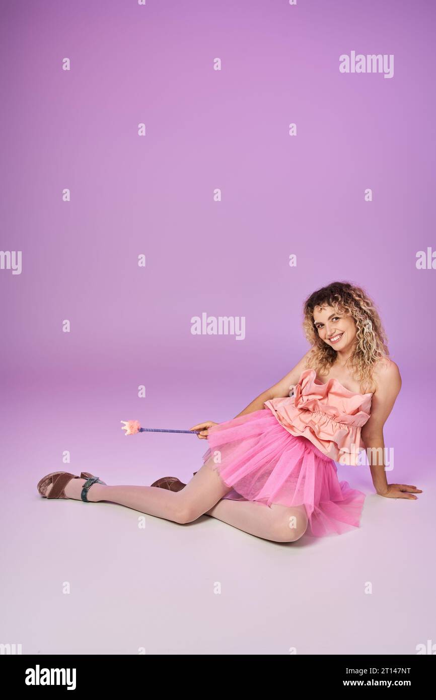 cheerful tooth fairy in vivid dress holding magic wand sitting on floor ...