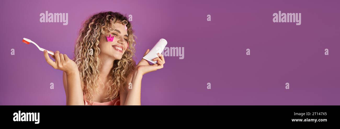 attractive cheerful woman with curly hair and face stickers holding ...