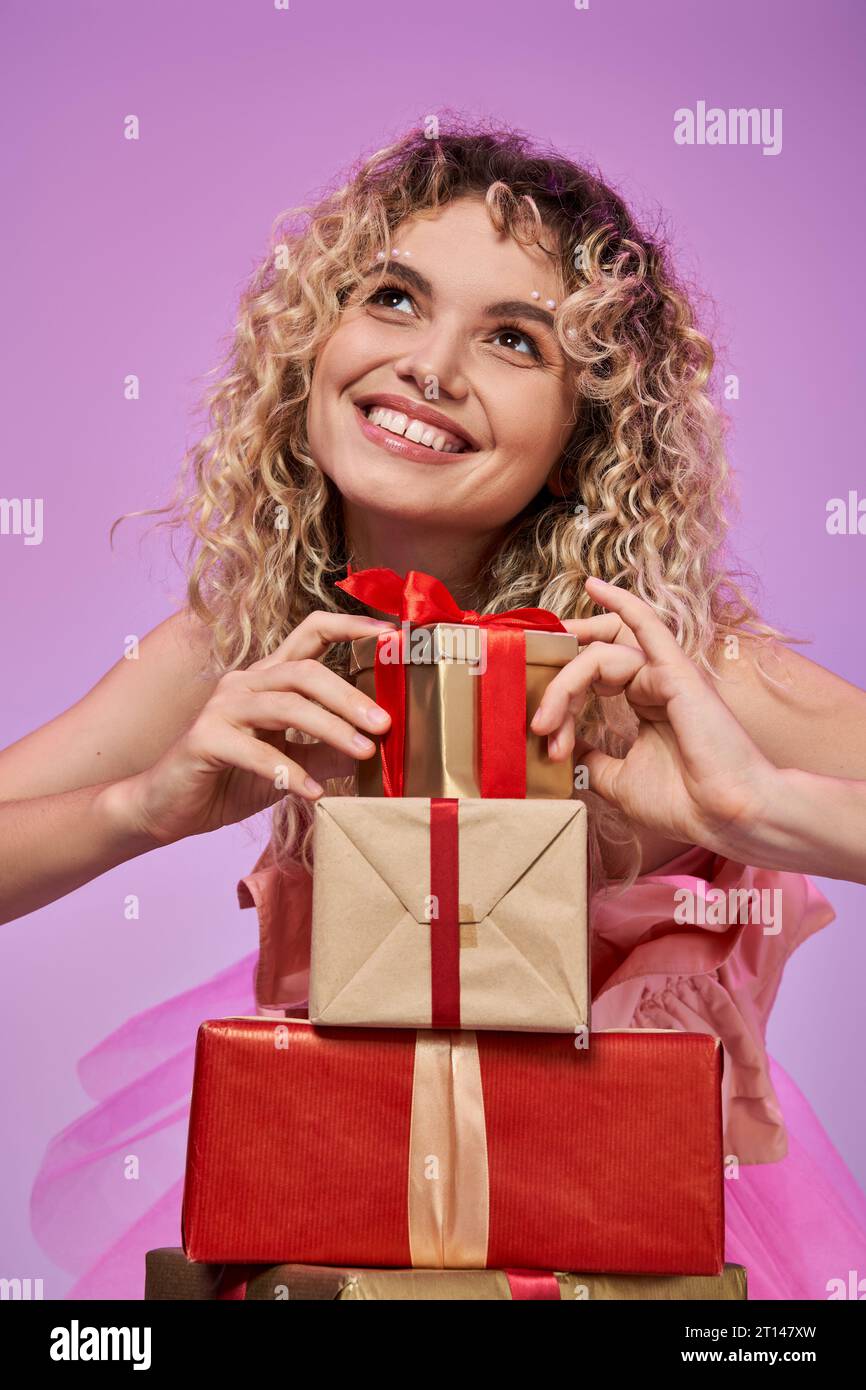 portrait of dreamy pretty woman with curly hair touching pile of gifts ...