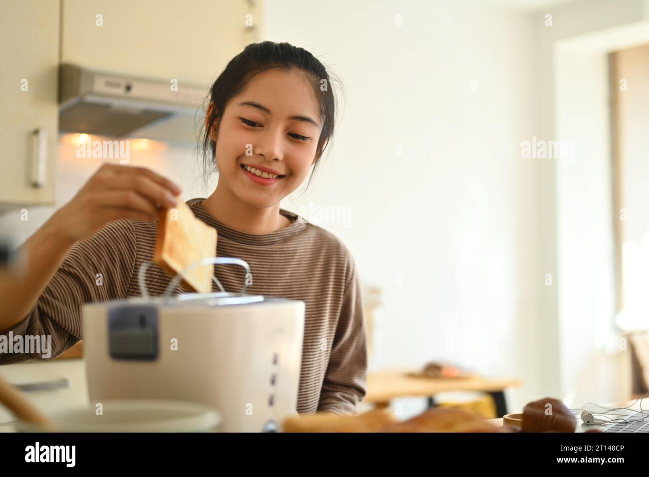Beautiful young woman preparing breakfast, toasting bread with toaster ...